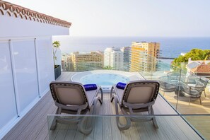 Uma varanda com hidromassagem, duas cadeiras e uma mesa de vidro.