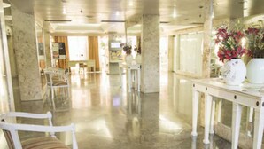 Um hall amplo com piso de mármore, mobiliário branco e um balcão de recepção com um vaso de flores.