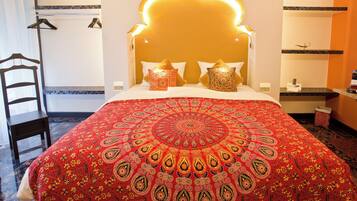 Quarto de hotel com uma cama grande, cabeceira com iluminação integrada, mesa de cabeceira com abajur e uma pequena prateleira com objetos decorativos.