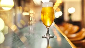 Um copo de cerveja sobre o balcão de um bar, com luzes e assentos ao fundo desfocados.