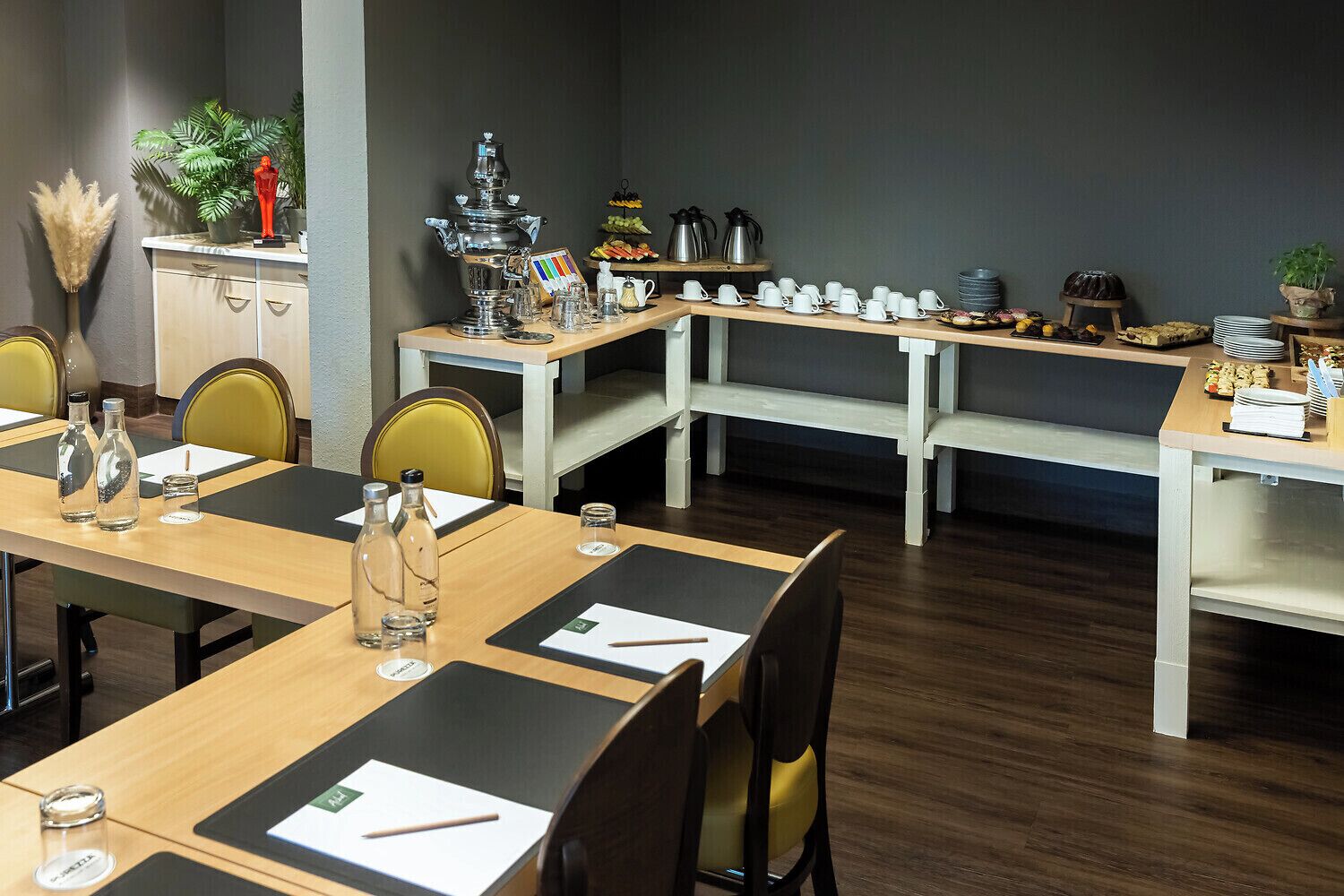 Sala de conferência com várias mesas, cadeiras e um espaço para buffet com diversos tipos de comida.