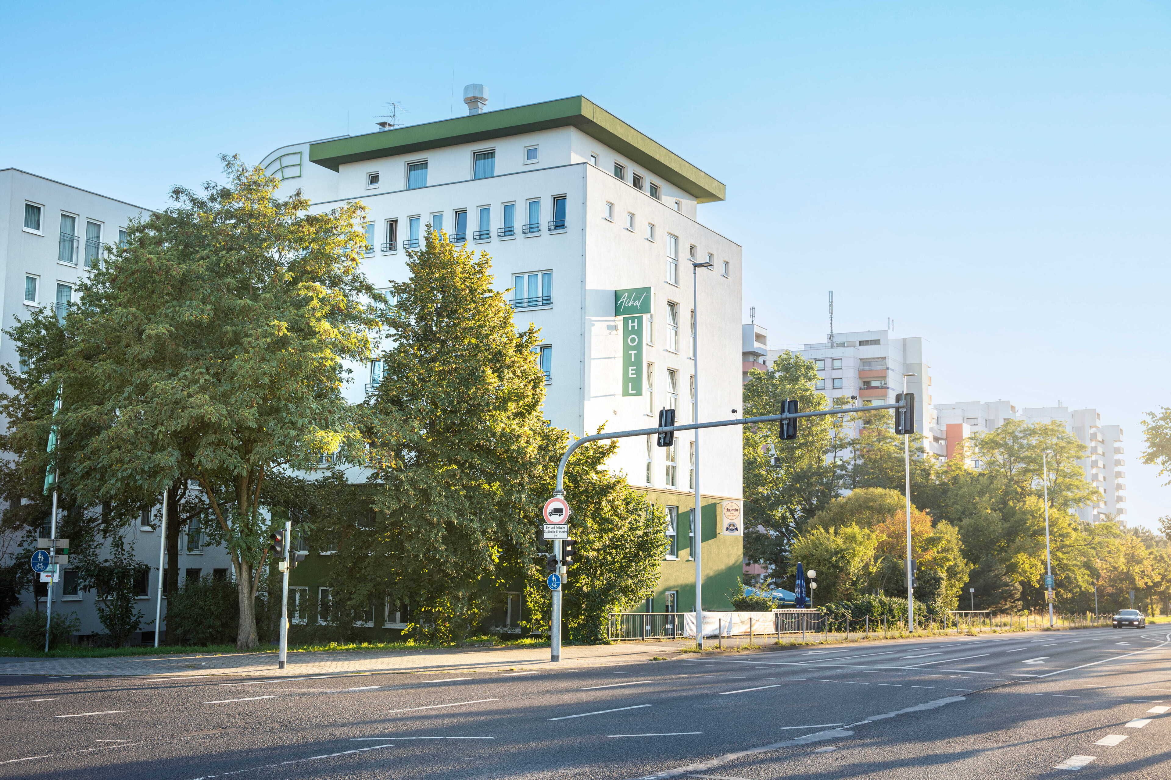Hotel de vários andares com telhado verde e fachada branca, situado no cruzamento de ruas.