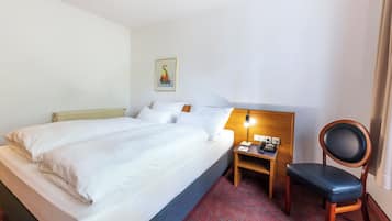 Quarto de hotel com cama, mesa de cabeceira, abajur, cadeira e um quadro na parede.