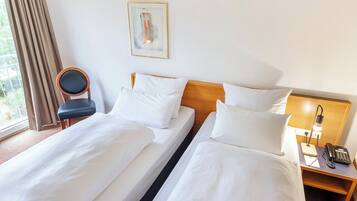 Quarto de hotel com duas camas, uma cadeira, mesa de cabeceira com abajur e um quadro na parede.