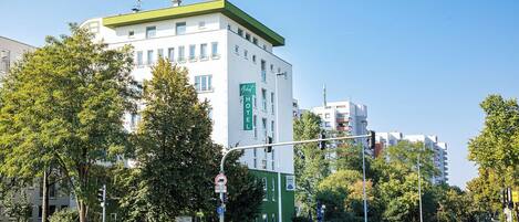 Um hotel com fachada verde e branca, vários andares e céu claro.
