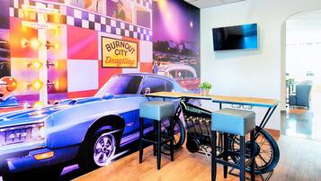 Quarto com um mural de carro de corrida de arrancada, área de bar com banquetas e uma televisão na parede.