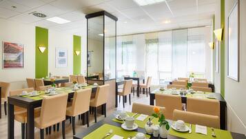Uma sala de jantar de hotel com várias mesas preparadas para o pequeno-almoço, equipada com conjuntos de chá e arranjos florais.