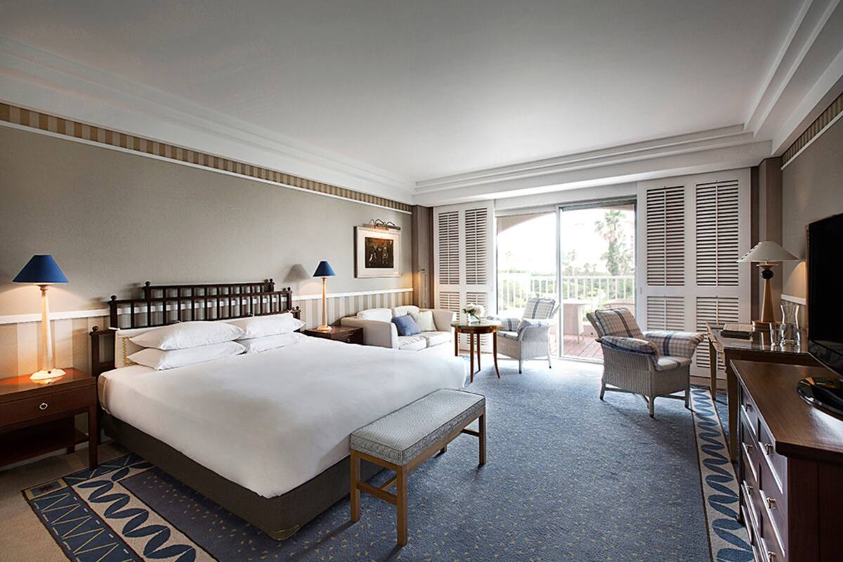 Quarto de hotel com uma cama grande, uma escrivaninha, uma cadeira, uma mesinha e uma televisão.
