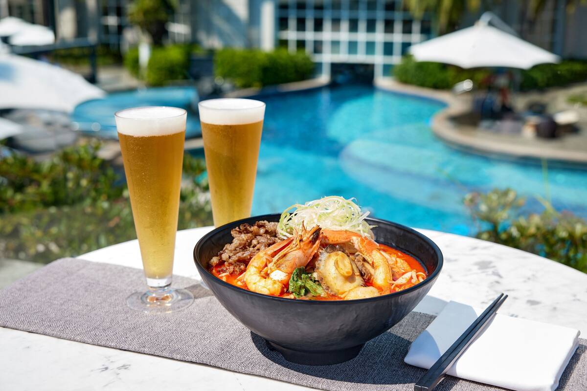Uma tigela de sopa de marisco com um copo de cerveja numa mesa junto a uma piscina.