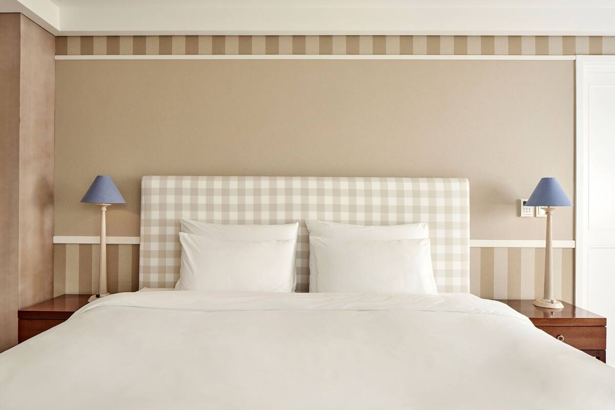 Uma cama bem arrumada com cabeceira xadrez, duas luminárias de cabeceira e uma parede com padrão listrado.
