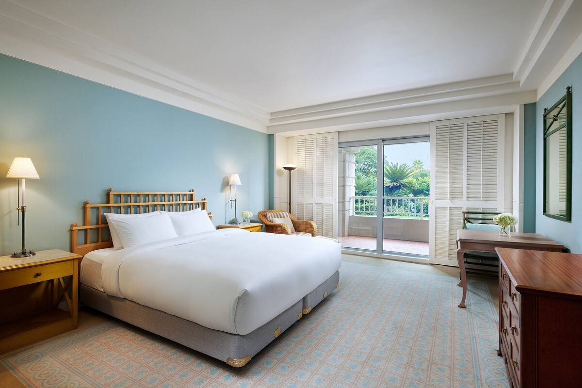 Quarto com uma cama grande, escrivaninha, cadeira e varanda com vista para o verde.