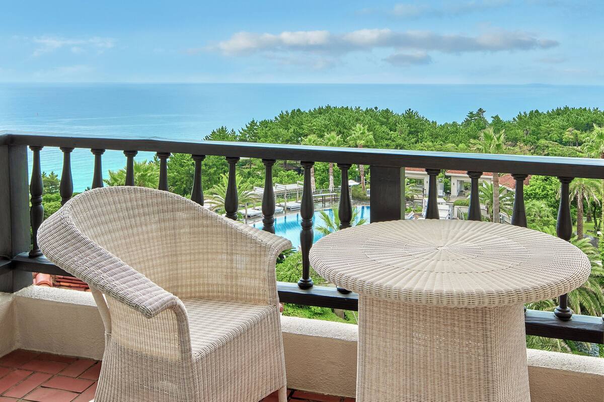 Varanda com móveis de vime com vista para uma piscina e para o oceano.