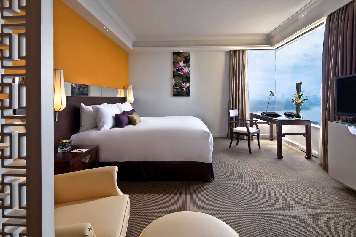 Quarto de hotel com cama grande, escrivaninha, cadeira e televisão.
