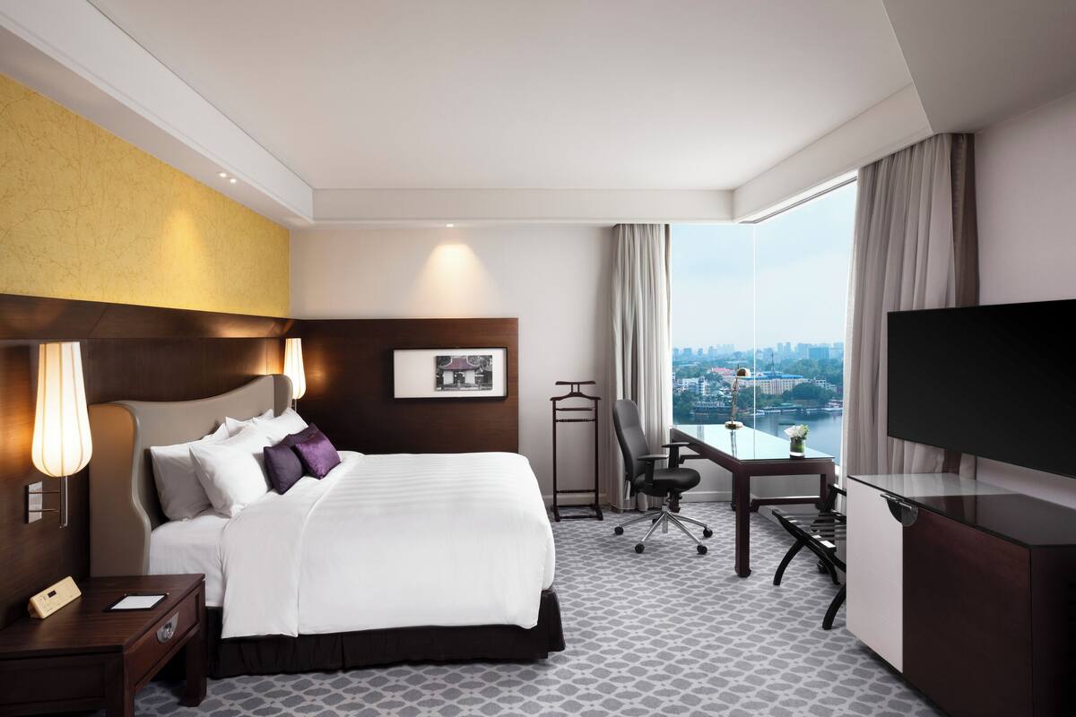 Quarto de hotel com cama, escrivaninha, cadeira, televisão e vista para a cidade.