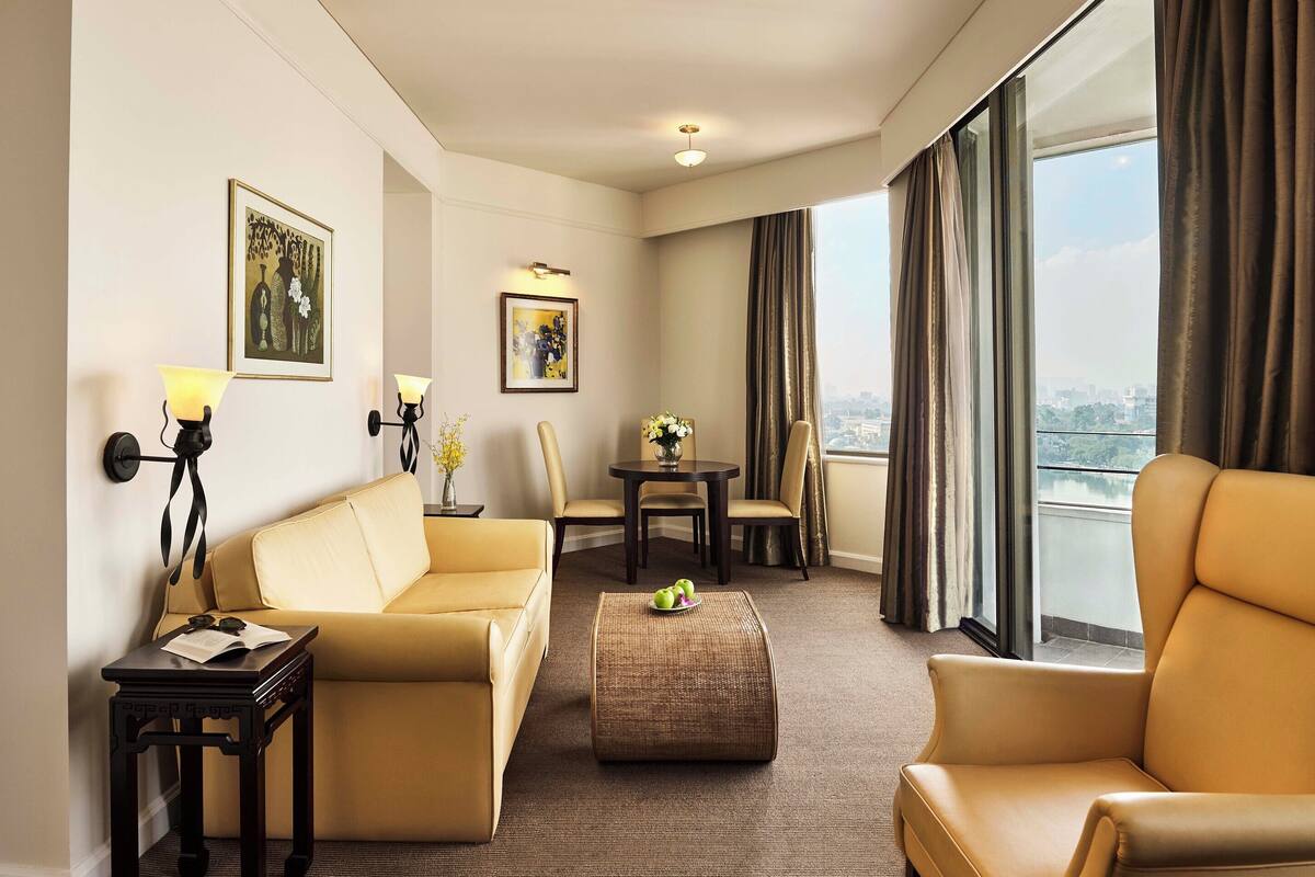 Quarto de hotel moderno com sofá, poltrona e uma pequena mesa com um vaso de flores.