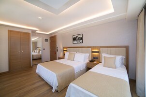 Quarto de hotel com duas camas, soalho em madeira, um guarda-roupa grande e um candeeiro de teto.