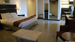Quarto de hotel com cama, mesa pequena, cadeira, escrivaninha e cozinha compacta.