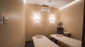Sala de spa com duas macas de massagem, pia e iluminação embutida na parede.