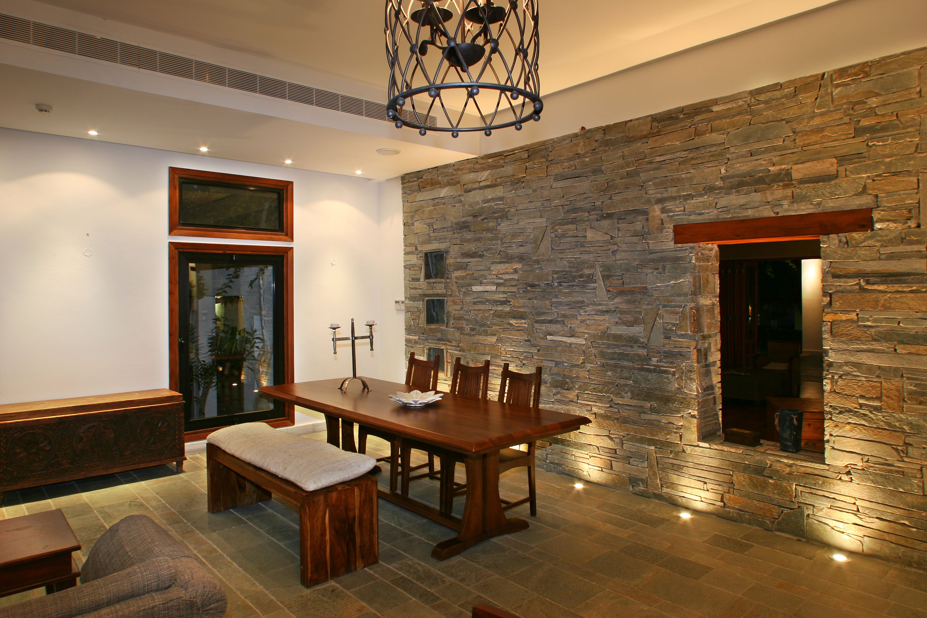 Uma sala de jantar com mesa e cadeiras de madeira, um banco e uma parede de pedra.