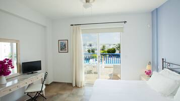 Quarto de hotel com cama, secretária com televisão, cadeira, varanda com vista para a cidade e janela com cortinas.
