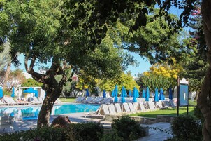 Uma área de piscina com espreguiçadeiras e guarda-sóis azuis, cercada por árvores e vegetação.