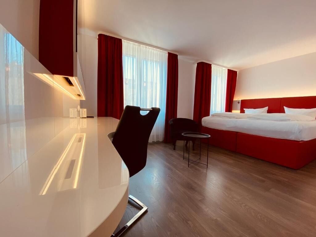 Quarto de hotel com cama, escrivaninha e cadeira.