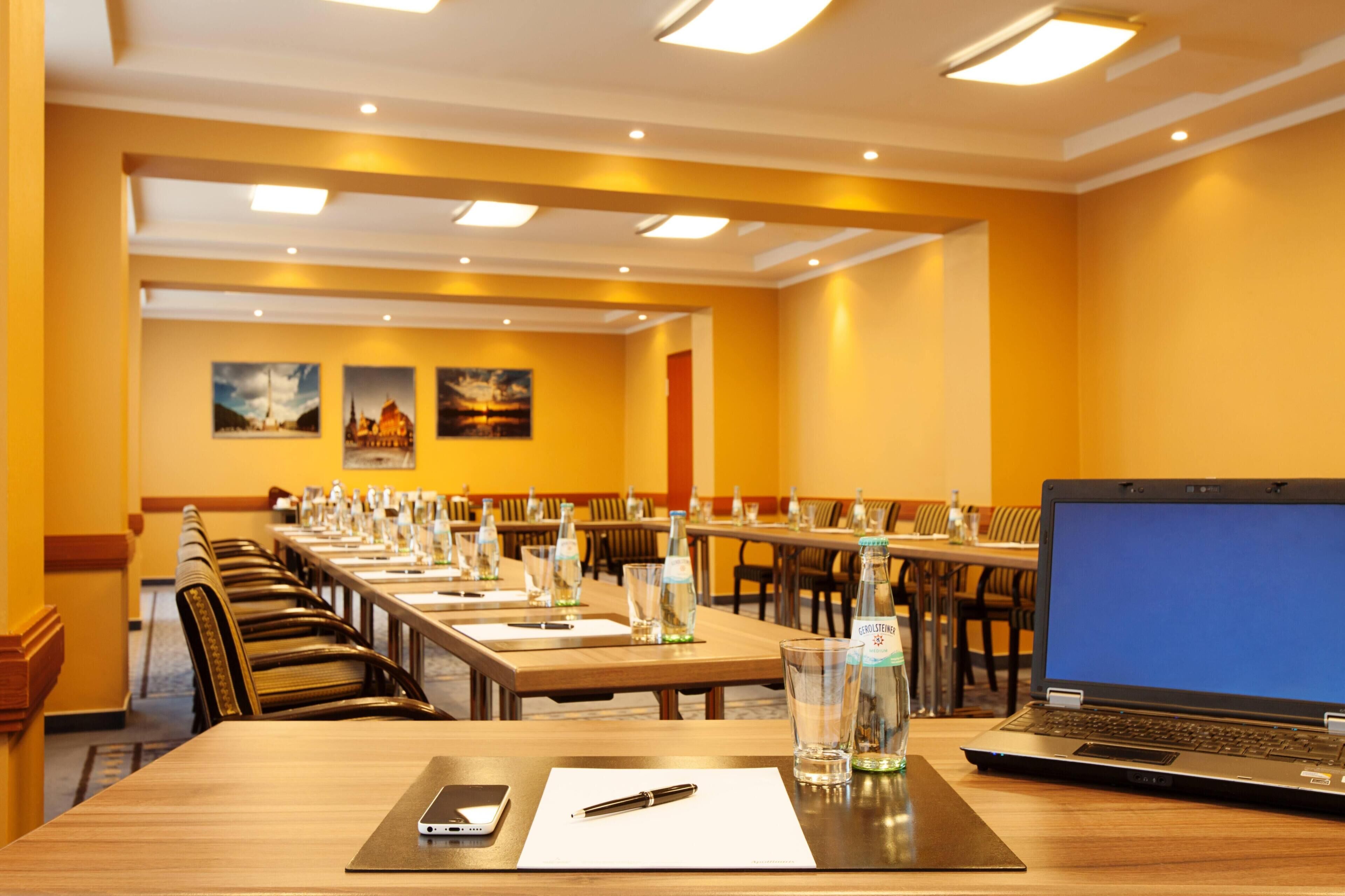 Uma sala de conferências com mesas compridas, cadeiras e um laptop em uma das mesas.