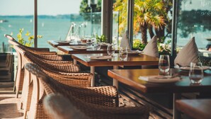 Restaurante com cadeiras de vime e mesas de madeira, com vista para um corpo d'água.