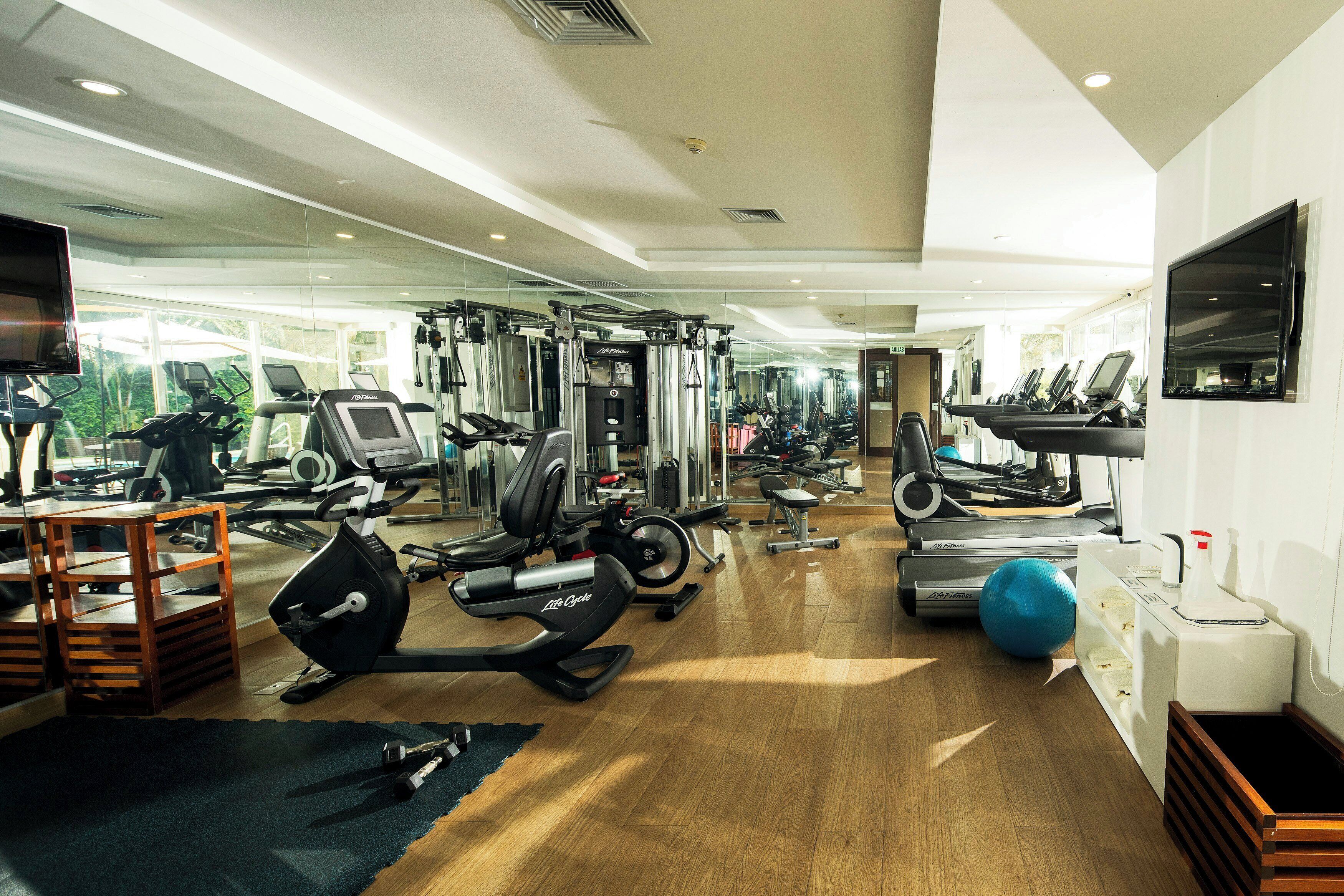 Academia com máquinas de cardio, equipamentos de musculação e um espelho grande.