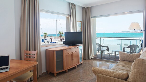 Quarto de hotel com varanda, televisão, secretária de madeira e sofá.
