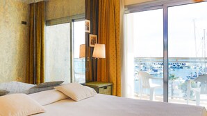 Quarto de hotel com uma cama grande, vista para uma marina e uma varanda com cadeiras.