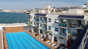 Um hotel com piscina, várias varandas com espreguiçadeiras e vista para o mar.