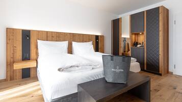 Quarto de hotel moderno com cabeceira de madeira, cama grande com lençóis brancos, mesa de cabeceira e guarda-roupa com espelho e prateleiras.