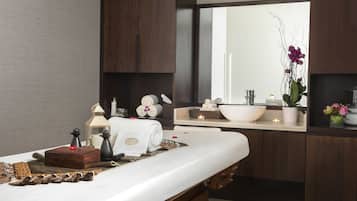 Uma sala de spa moderna com um espelho grande, uma bacia branca e uma mesa de massagem.