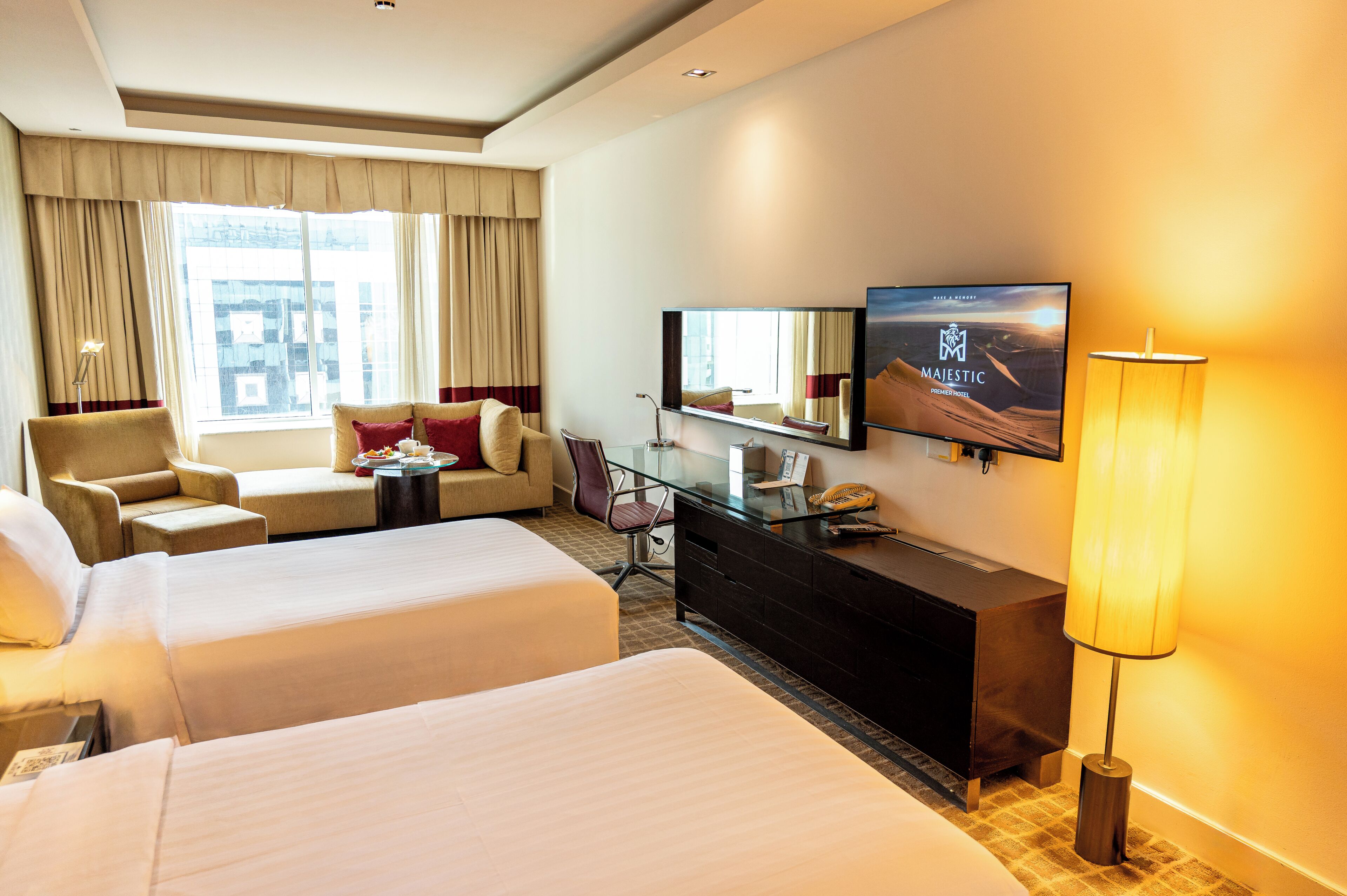 Quarto de hotel com duas camas, uma escrivaninha, uma cadeira, uma TV e um abajur.