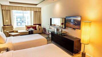 Quarto de hotel com duas camas, uma escrivaninha, uma cadeira, uma TV e um abajur.