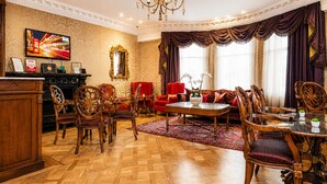Uma sala de estar ampla com um grande candelabro, sofás vermelhos, cadeiras de madeira, lareira e uma televisão na parede.
