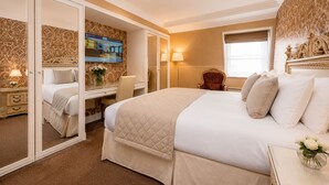 Quarto de hotel com uma cama grande, uma escrivaninha, uma cadeira, um guarda-roupa e uma janela.