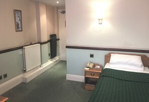 Quarto de hotel com cama, mesa de cabeceira, luminária e radiador.