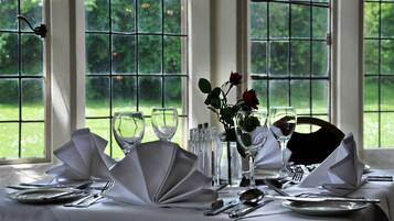 Uma mesa posta para refeição com vista para um jardim através de grandes janelas.