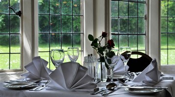 Uma mesa posta para refeição com vista para um jardim através de grandes janelas.