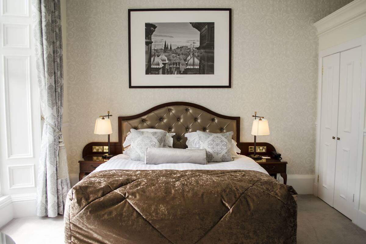 Quarto bem organizado com cama grande, duas mesas de cabeceira com abajures, um quadro na parede e um guarda-roupa.