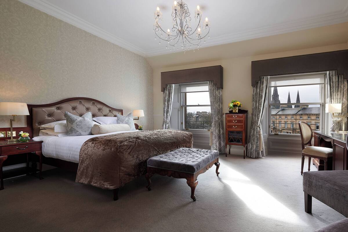 Um quarto espaçoso com uma cama grande, um espaço de estar com uma poltrona e vista para a cidade pela janela.