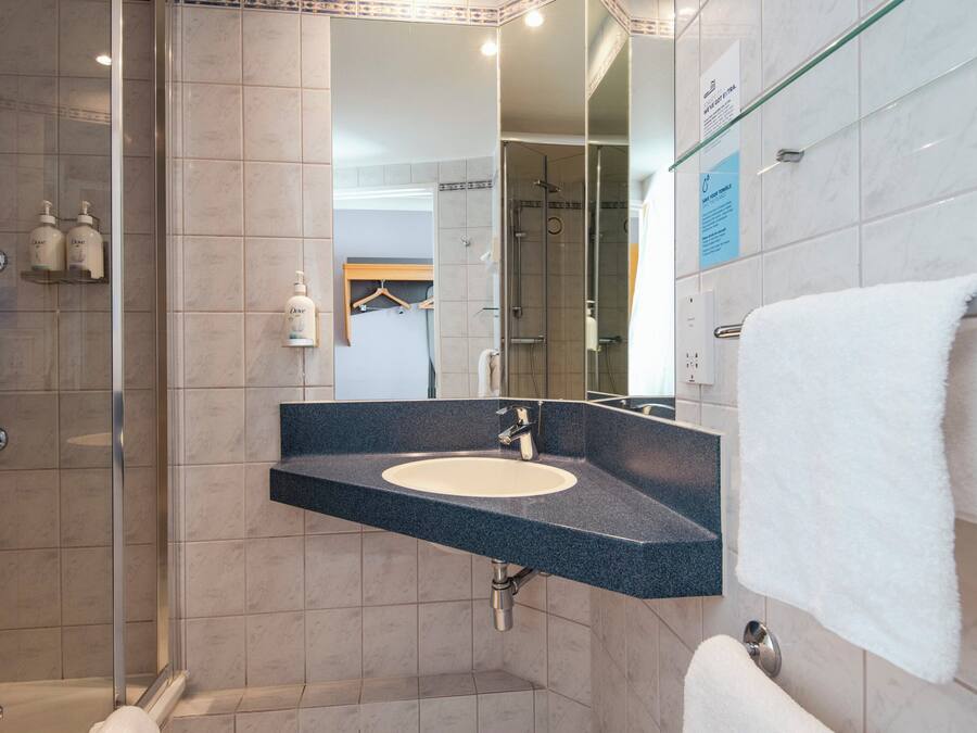 Uma casa de banho moderna com cabine de chuveiro em vidro, uma pia com bancada escura e um porta-toalhas.
