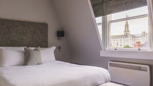 Quarto de hotel com cama, cabeceira, janela com vista para um edifício e termostato.