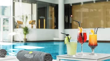 Mesa à beira da piscina com três bebidas, uma toalha e vista para a área da piscina.