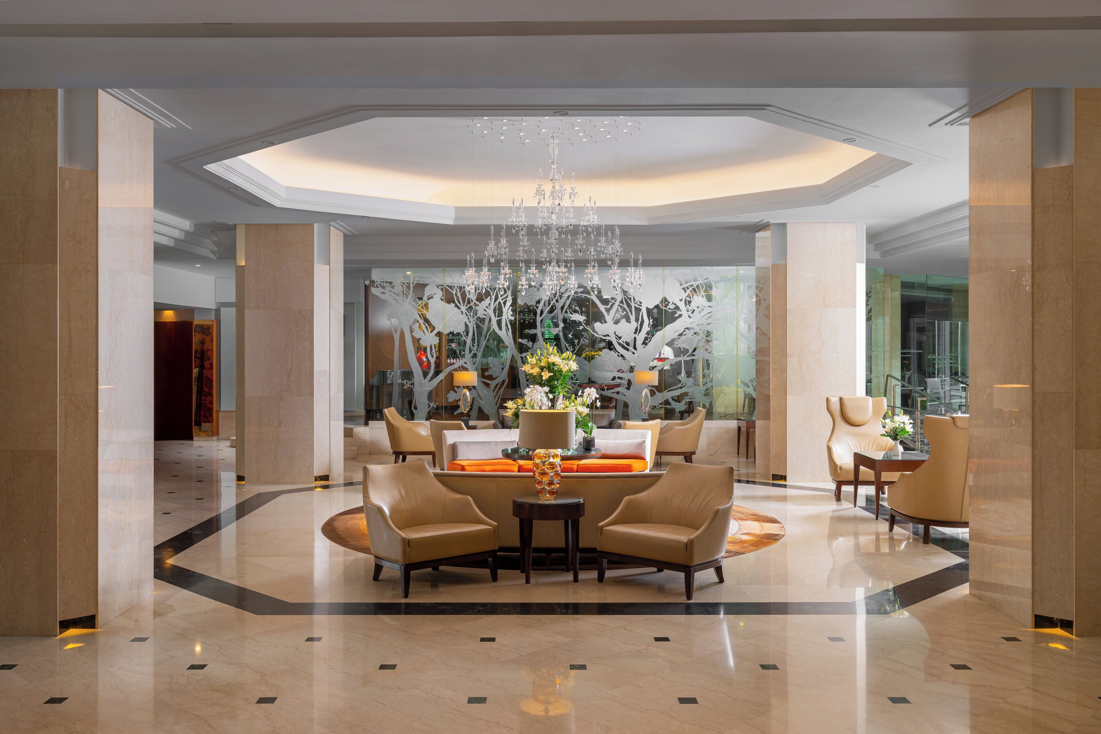 Um hall espaçoso com área de refeições central, um candelabro e uma parede de vidro com uma árvore decorativa.