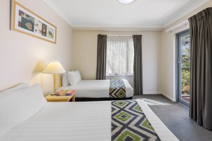 Quarto de hotel com duas camas, janela com cortinas, luminária e quadro pendurado na parede.