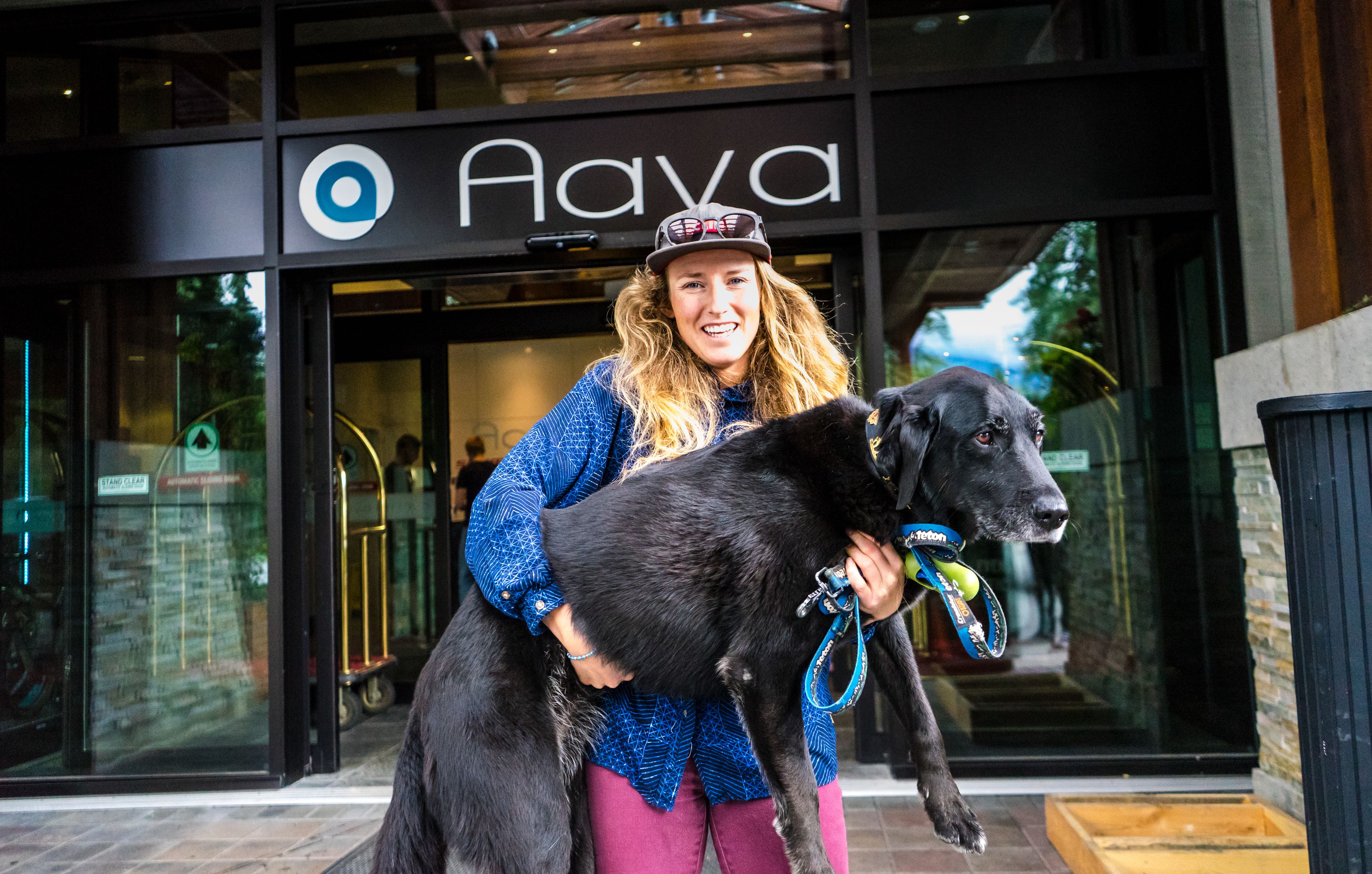 Uma pessoa segurando um cão preto grande em frente a um edifício com uma placa que diz "Ava".