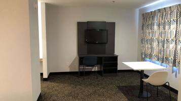 Quarto pequeno e moderno, com escrivaninha, cadeira e televisão de tela plana na parede.